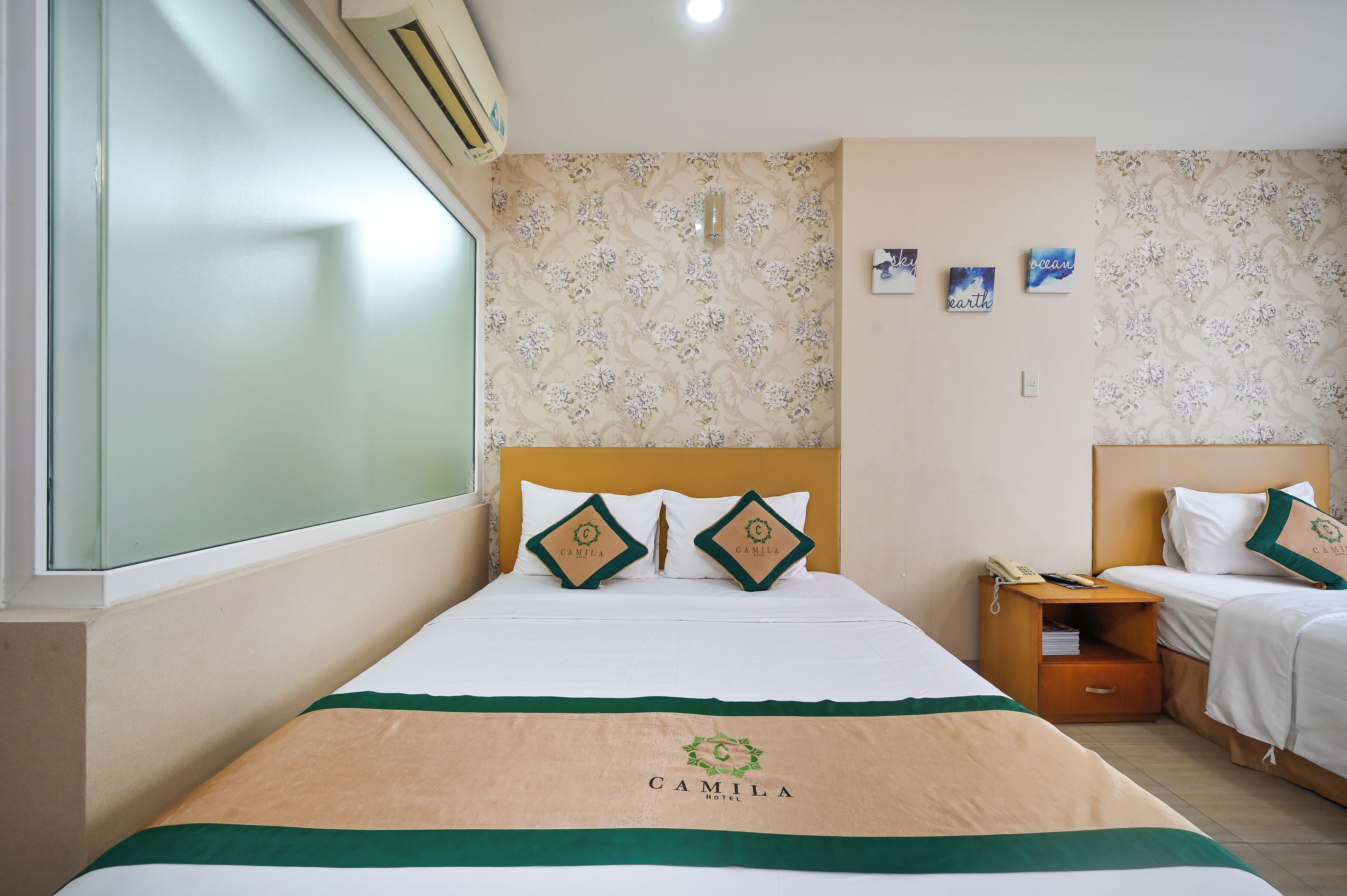 Quarto de hotel com uma cama, uma mesa de cabeceira, uma janela e uma parede com quadros.