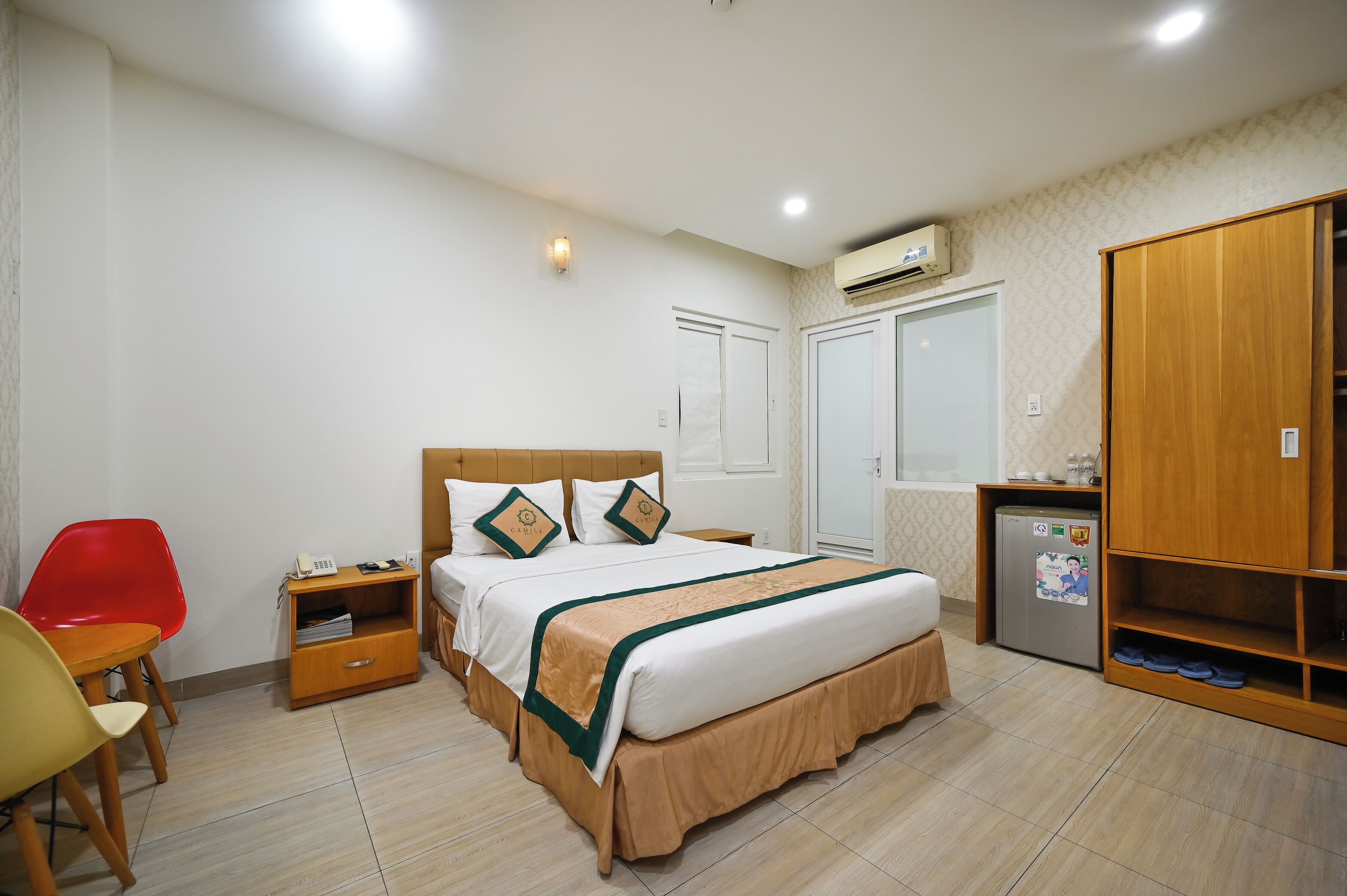 Quarto de hotel com cama, escrivaninha, cadeira, armário e um pequeno frigorífico.