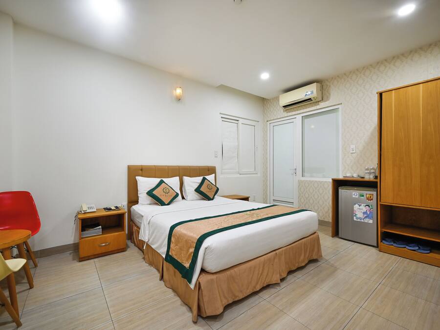 Quarto de hotel com cama, escrivaninha, cadeira, armário e um pequeno frigorífico.