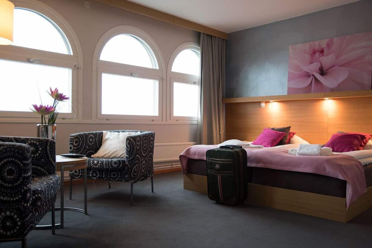 Quarto de hotel com cama, uma cadeira, uma mesa e um vaso com flores.
