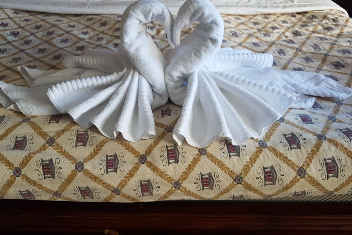 Uma cama com um edredom estampado e duas toalhas dobradas em forma de cisne.