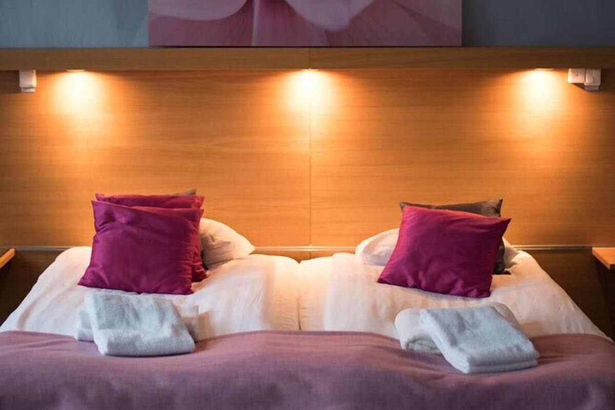 Uma cama de casal com duas almofadas, uma cabeceira de madeira e uma grande obra de arte floral acima.