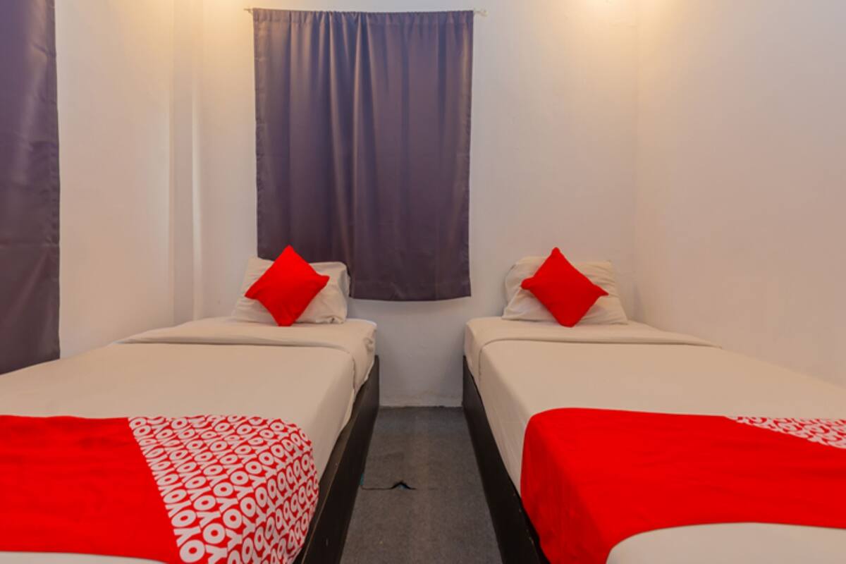 Quarto com duas camas, cada uma com travesseiro vermelho e manta estampada.
