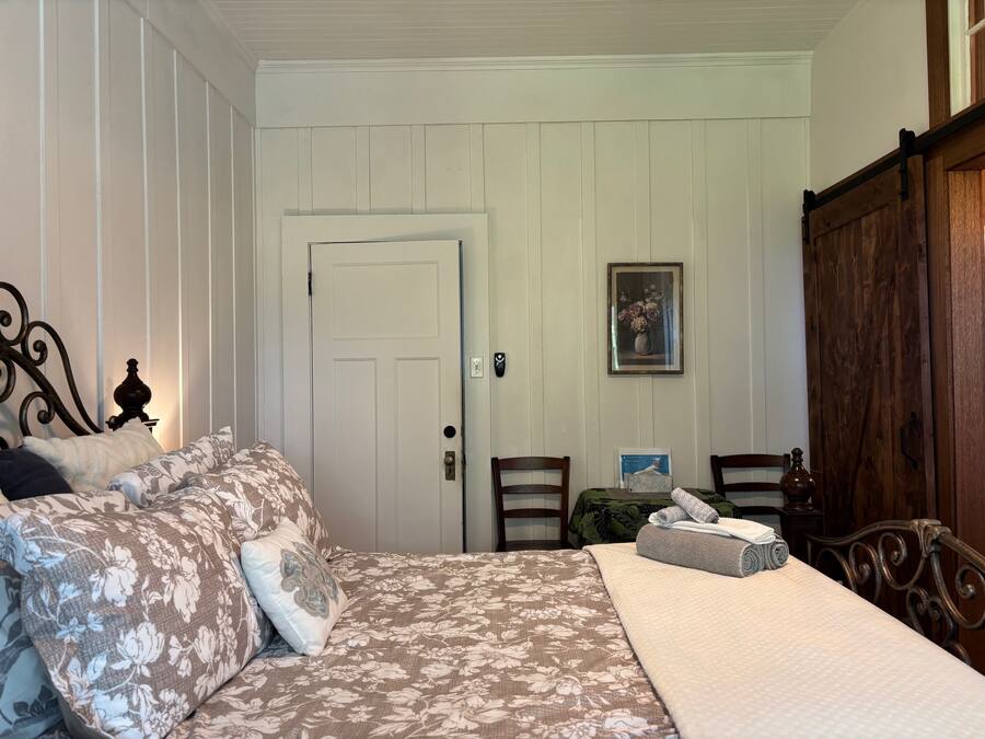 Quarto com uma cama, duas cadeiras, um guarda-roupa de madeira, uma porta branca e um quadro na parede.