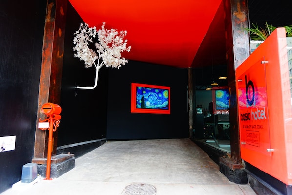 Entrada de hotel com teto vermelho, uma obra de arte emoldurada e uma placa com a inscrição 'basic hotel'.