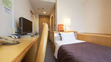 Quarto de hotel com cama, mesa de cabeceira, abajur e escrivaninha com computador e telefone.