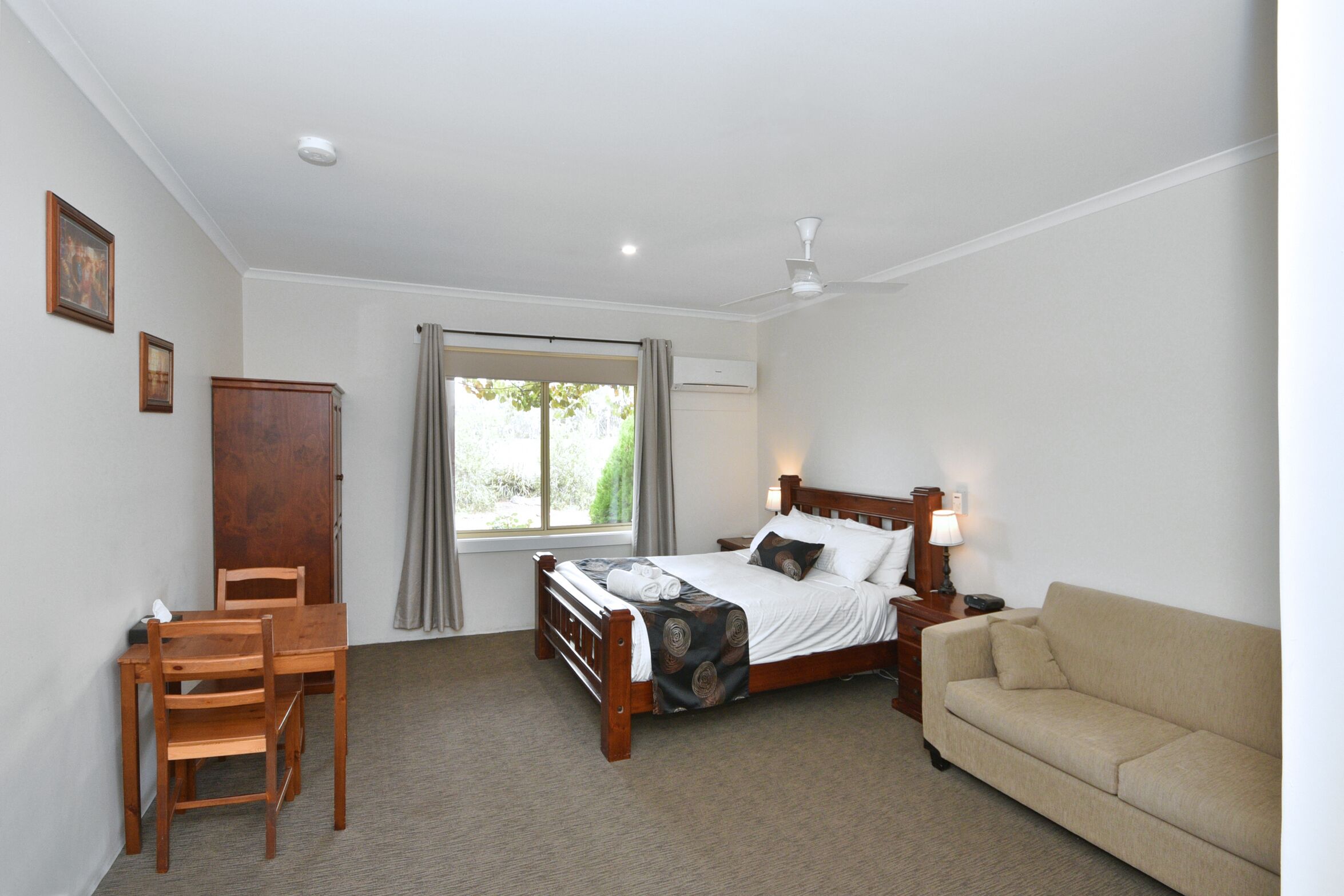 Quarto com cama, cadeira de madeira, sofá, escrivaninha e janela com cortinas.