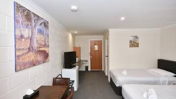 Quarto de hotel com uma cama, uma escrivaninha com televisão, um quadro na parede e uma porta que dá para outro espaço.