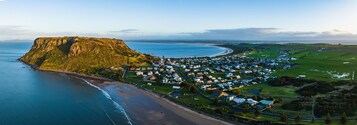 Vista aérea de uma cidade costeira com uma colina imponente, uma praia e um conjunto de casas.