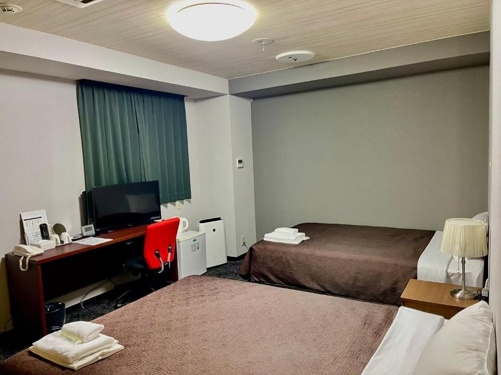 Quarto de hotel com duas camas, uma escrivaninha com computador, televisão e telefone.