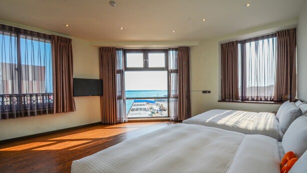 Quarto de hotel com duas camas, uma janela grande com cortinas e vista para uma marina.