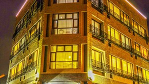 Um hotel de vários andares com uma placa grande no topo, janelas amplas em cada andar e uma entrada visível com rampa.
