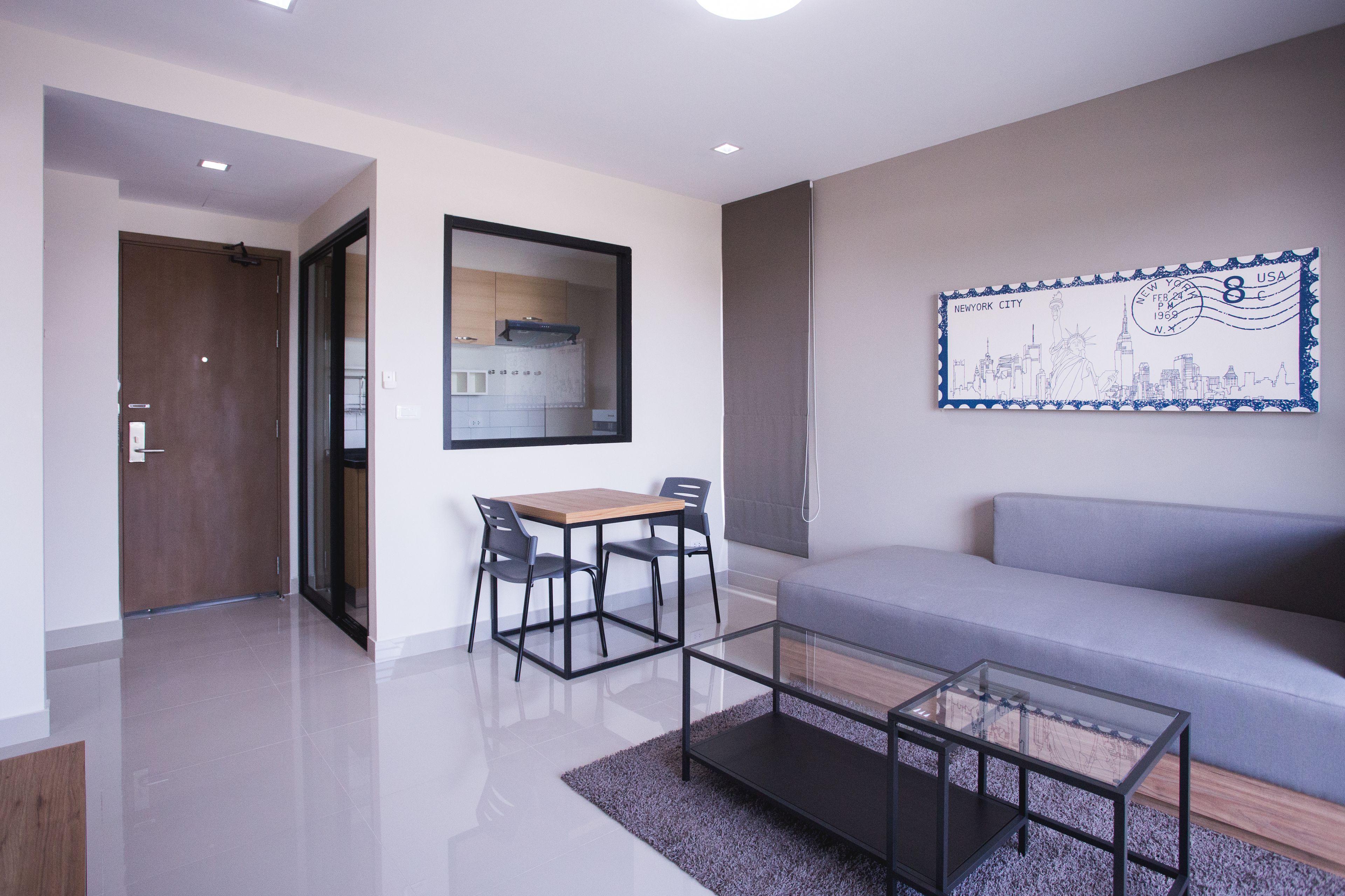 Uma sala de estar moderna com um sofá, uma mesa de centro de vidro, uma mesa de jantar com cadeiras, um espelho e uma obra de arte com uma paisagem urbana emoldurada na parede.