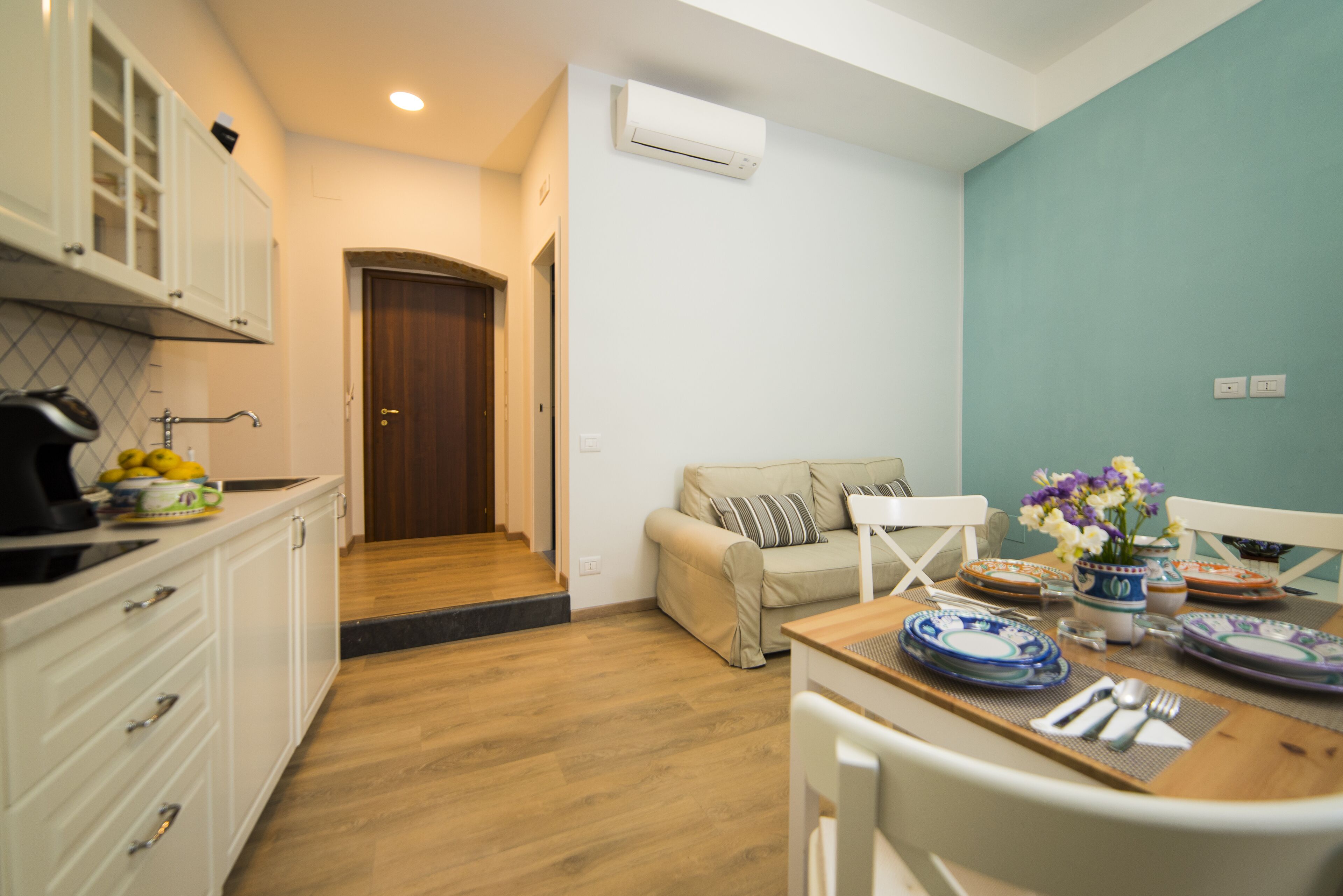 Cozinha compacta com armários brancos, bancada de madeira e um espaço de refeições com mesa posta para dois.