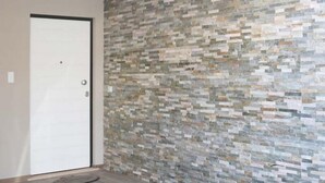 Um quarto com porta branca, parede de pedra texturizada e chão cinzento.