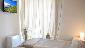 Quarto com duas camas, uma TV na parede, aquecedor e abajur na mesinha de cabeceira.