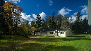 Uma casa de dois andares com garagem, cercada por um gramado e árvores.