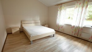Quarto com cama, mesa de cabeceira, cômoda e janela com cortinas florais.