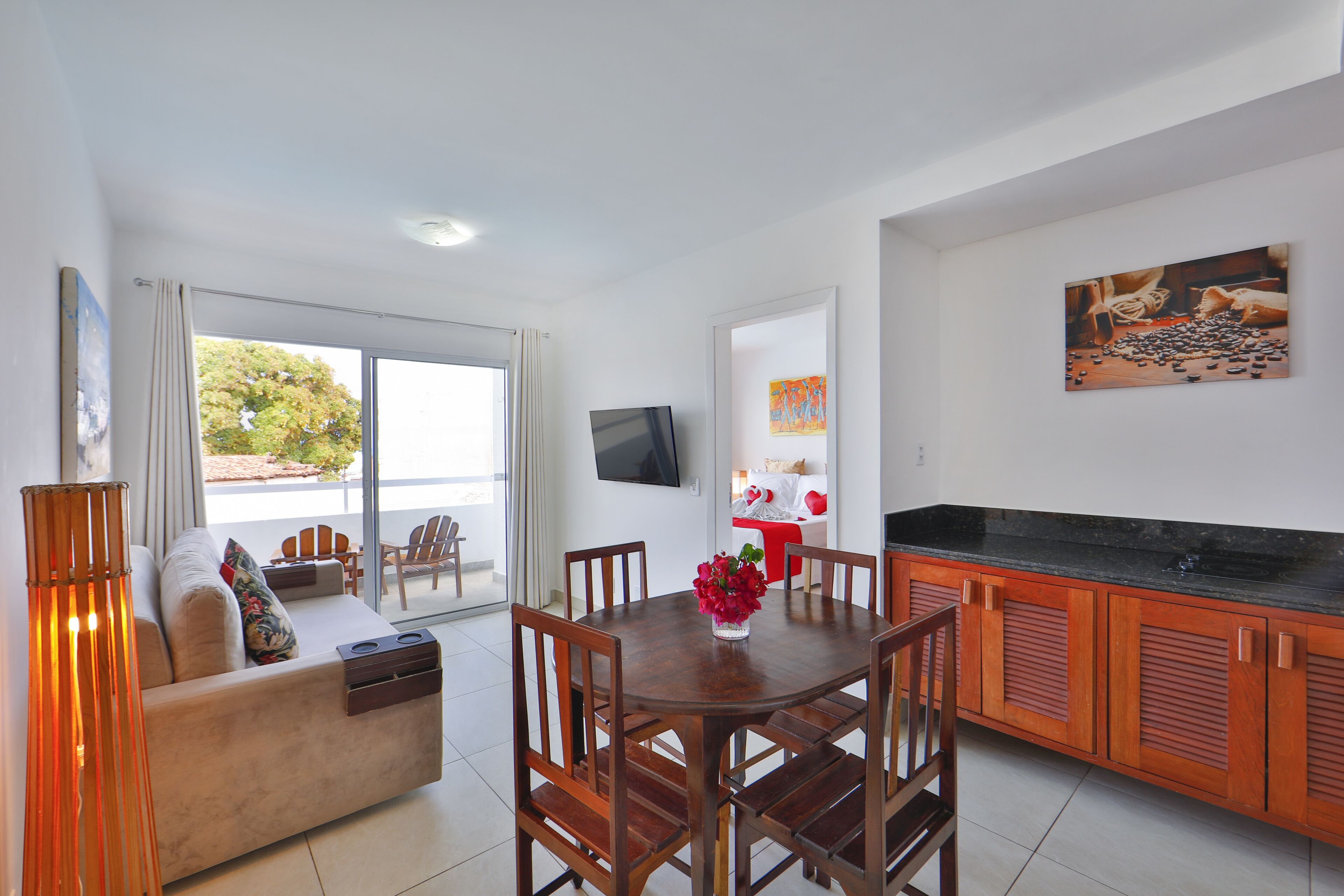 Uma sala de estar moderna com um sofá, uma mesa de jantar com cadeiras, uma área de cozinha com armários e uma televisão fixada na parede.
