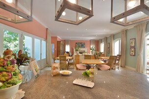 Uma ampla sala de jantar com uma grande mesa de granito, cadeiras de vime e vista para o exterior através de grandes janelas.