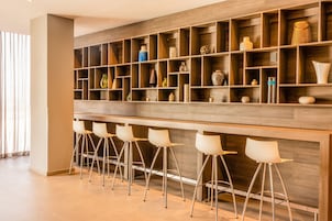 Uma área de bar moderna com um expositor de prateleiras de madeira e cinco banquetas brancas.