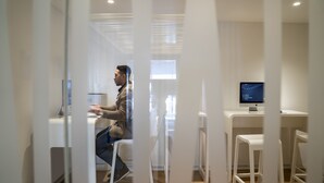 Um espaço de escritório moderno com uma pessoa trabalhando em uma mesa, móveis brancos e um monitor de computador exibindo uma lista.