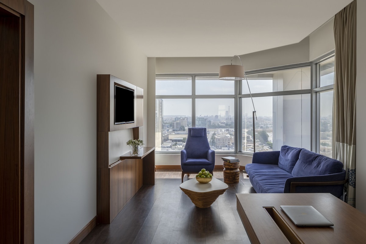 Uma sala de estar moderna com uma grande janela, um sofá, uma mesa de centro e uma televisão.