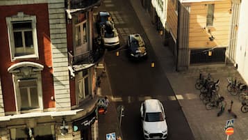 Vista da rua com um carro branco estacionado numa faixa de pedestres, edifícios com varandas e bicicletas encostadas no passeio.