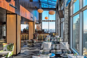 Uma área de estar moderna com assentos, bar e grandes janelas com vista para a cidade.