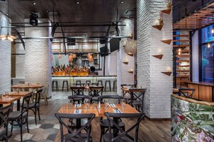 Interior de restaurante com paredes de tijolo, mesas de madeira e luminárias pendentes.