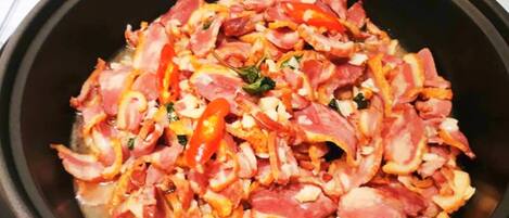 Uma frigideira preta com bacon cozido, pimentões vermelhos e cebolas.