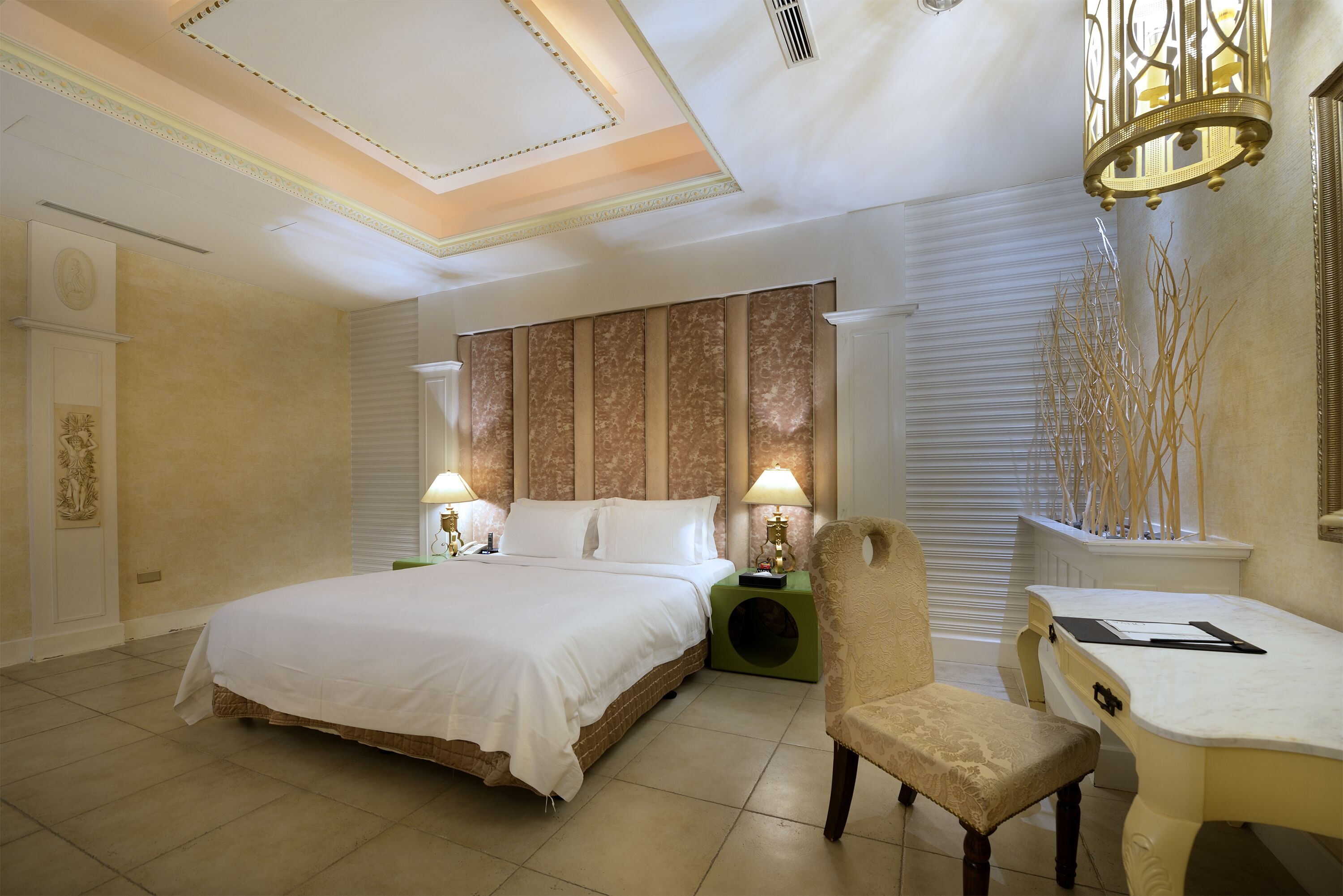Quarto de hotel com uma cama grande, duas mesas de cabeceira com luminárias, uma cadeira e uma escrivaninha.