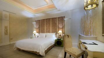 Quarto de hotel com uma cama grande, duas mesas de cabeceira com luminárias, uma cadeira e uma escrivaninha.