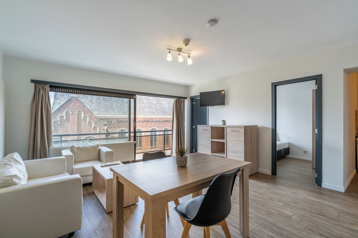 Uma sala de estar moderna com um sofá, uma mesa de jantar e uma TV fixada na parede.