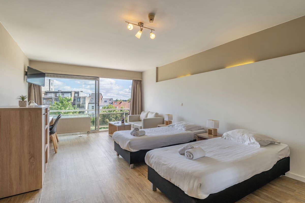 Quarto de hotel moderno com duas camas, uma escrivaninha e uma janela grande com vista para a cidade.
