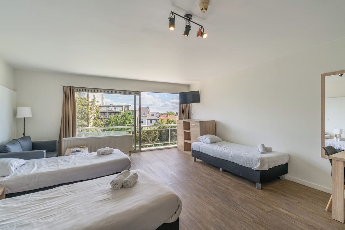 Quarto de hotel moderno com duas camas, televisão, secretária e varanda com vista para a cidade.