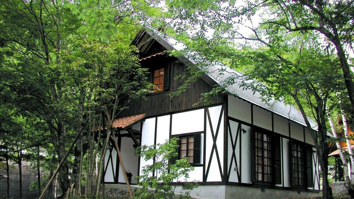 Um edifício tradicional em estilo de enxaimel com telhado inclinado, rodeado por vegetação verde exuberante.
