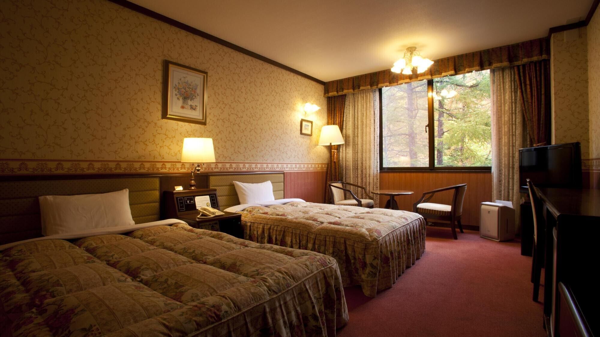 Quarto de hotel com duas camas, uma escrivaninha, uma cadeira, uma televisão e uma janela com cortinas.
