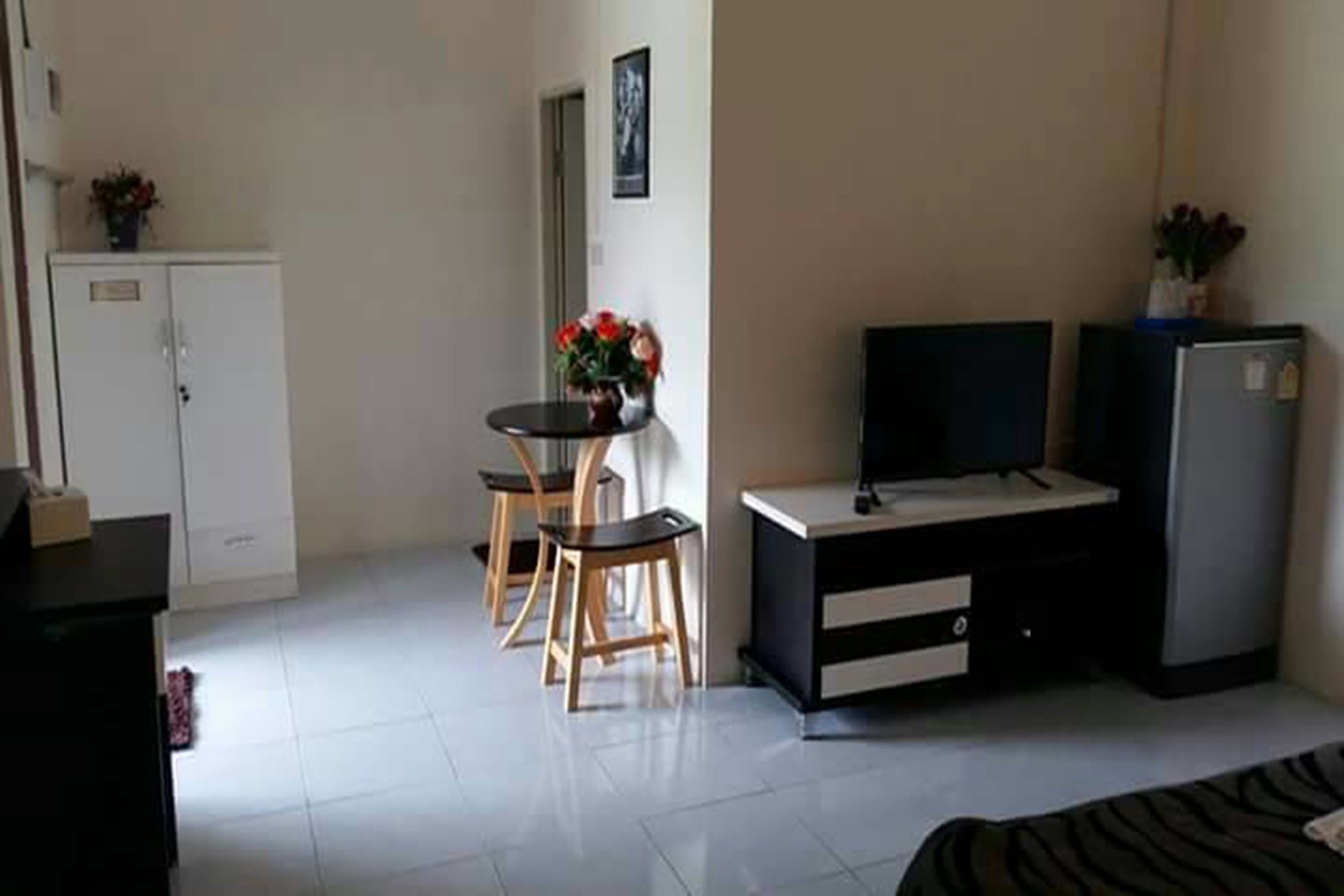 Quarto pequeno e limpo, com cama, escrivaninha, cadeira, televisão e frigorífico.