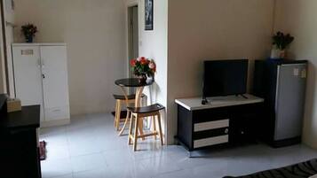 Quarto pequeno e limpo, com cama, escrivaninha, cadeira, televisão e frigorífico.