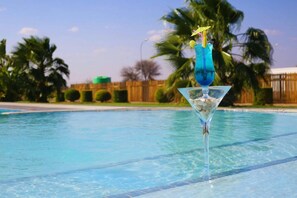 Piscina azul cristalina com uma taça de martini contendo uma bebida azul e um guarda-sol amarelo na borda.