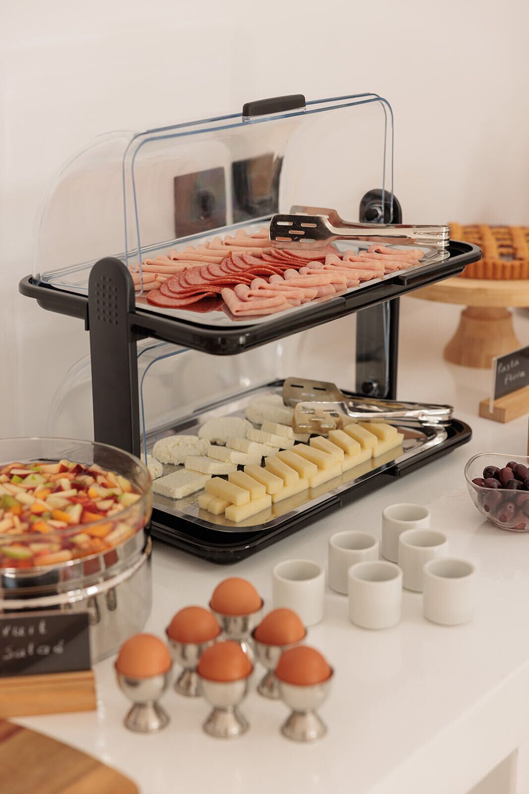 Uma mesa de buffet com diversos alimentos, incluindo carnes fatiadas, queijos e uma salada.