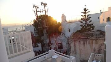 Terraço no telhado com mesa e cadeiras, com vista para uma cidade costeira com uma igreja e um edifício branco com um campanário.