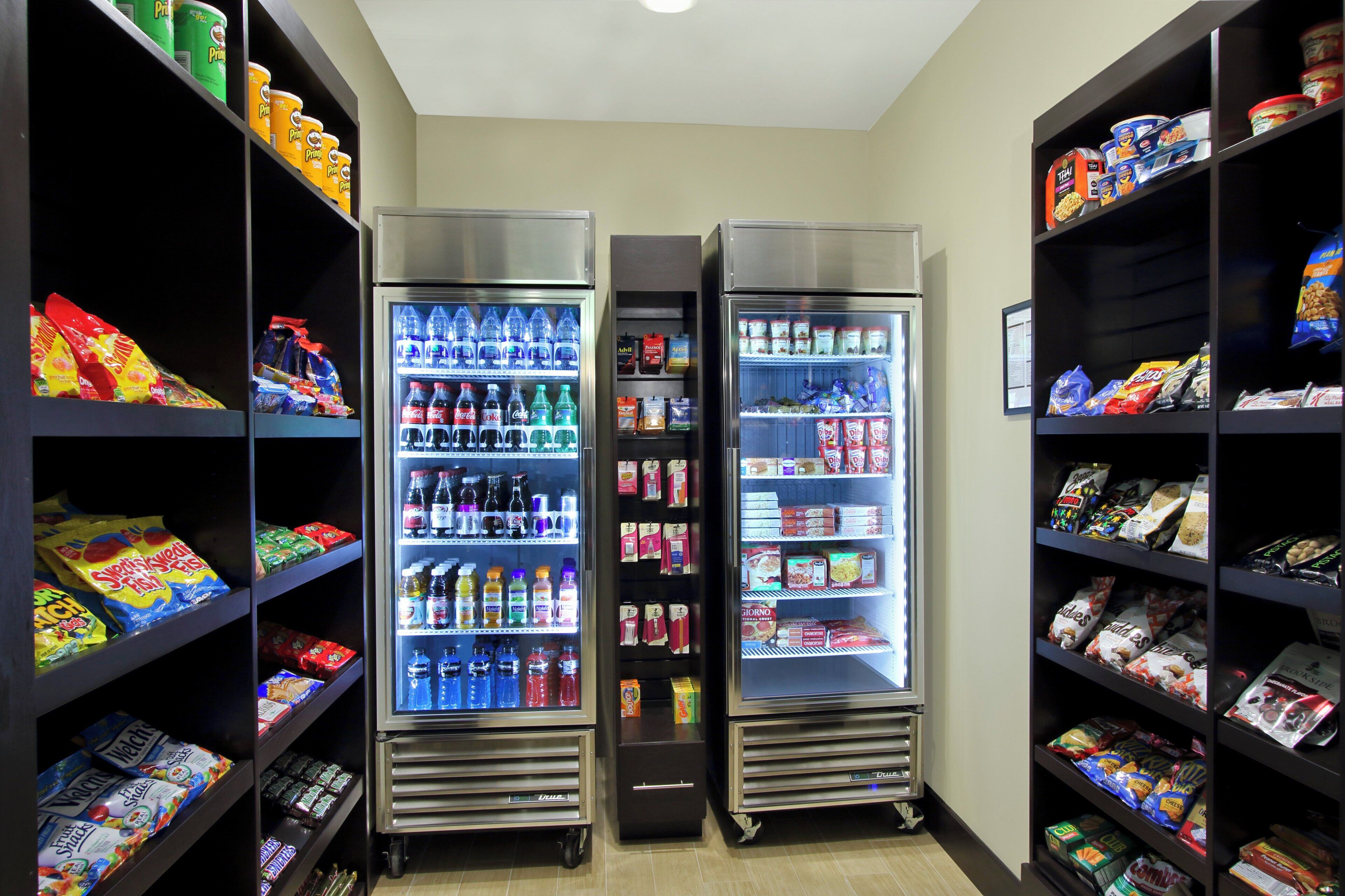 Uma área de máquinas automáticas com diversas opções de bebidas e lanches, incluindo água engarrafada, refrigerantes e vários salgadinhos embalados.
