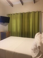 Quarto com cama, televisão de tela plana na parede e mesa de cabeceira de madeira com recipiente de vidro.