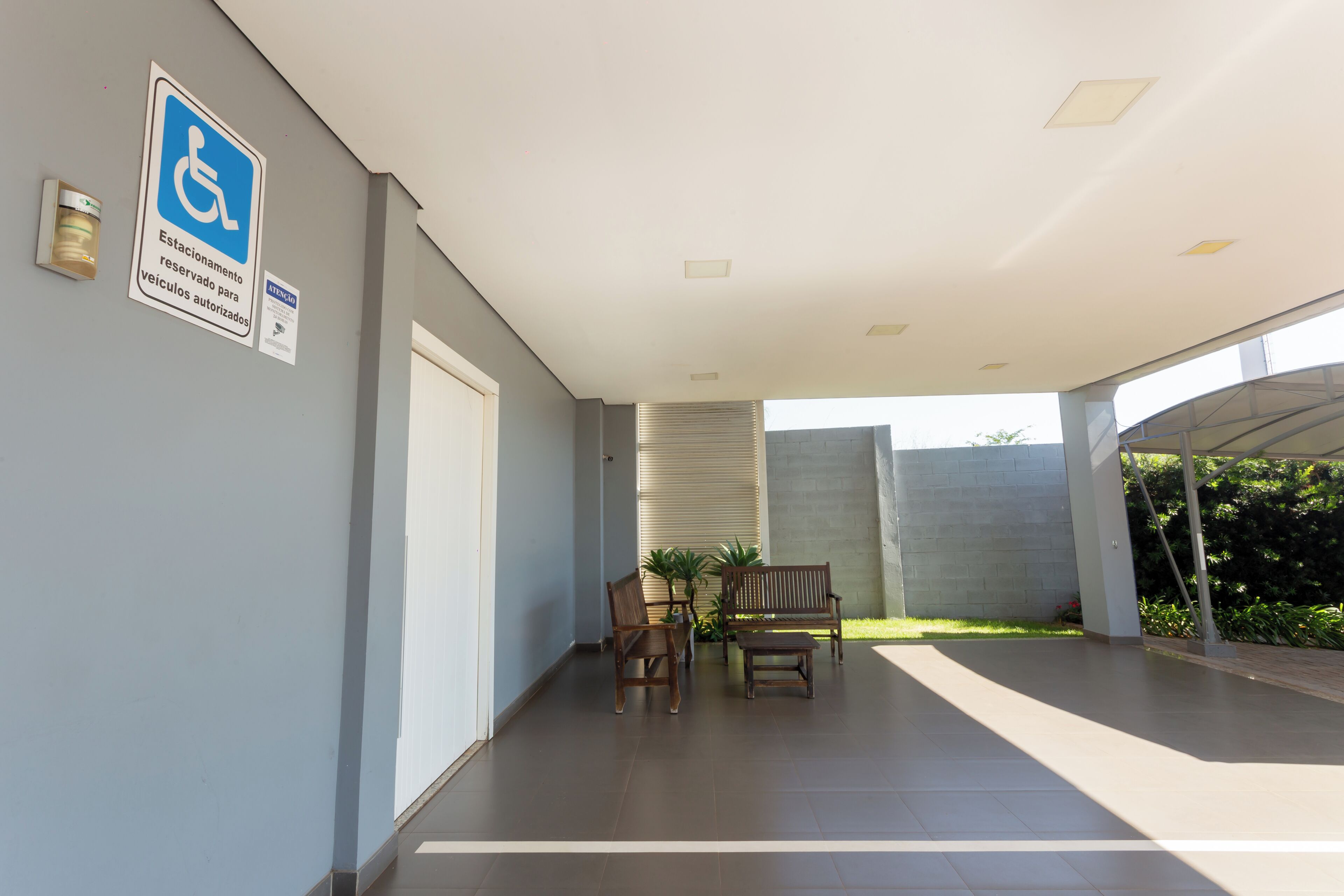 Uma área externa coberta com sinalização de acessibilidade para cadeiras de rodas, um banco e uma mesa.