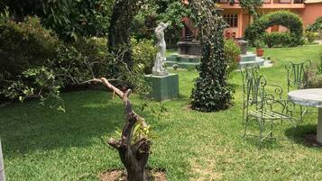 Um jardim com uma estátua, uma árvore pequena e um edifício ao fundo.