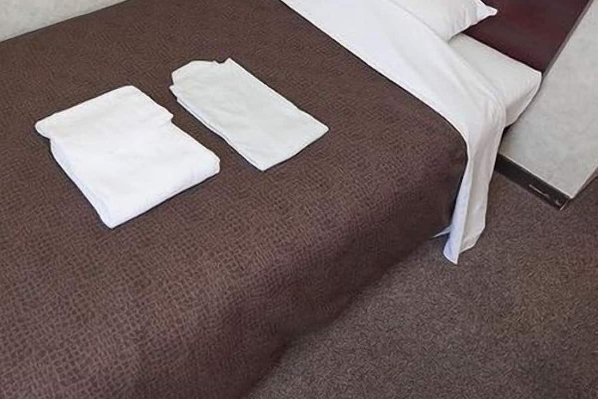Uma cama com um espalha dourado, almofadas brancas e duas toalhas brancas.