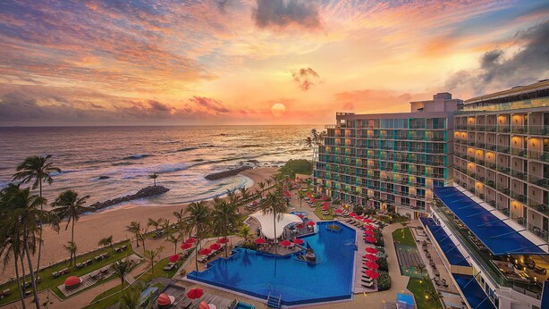 Resort com uma piscina grande, acesso à praia e vista para o oceano ao pôr do sol.