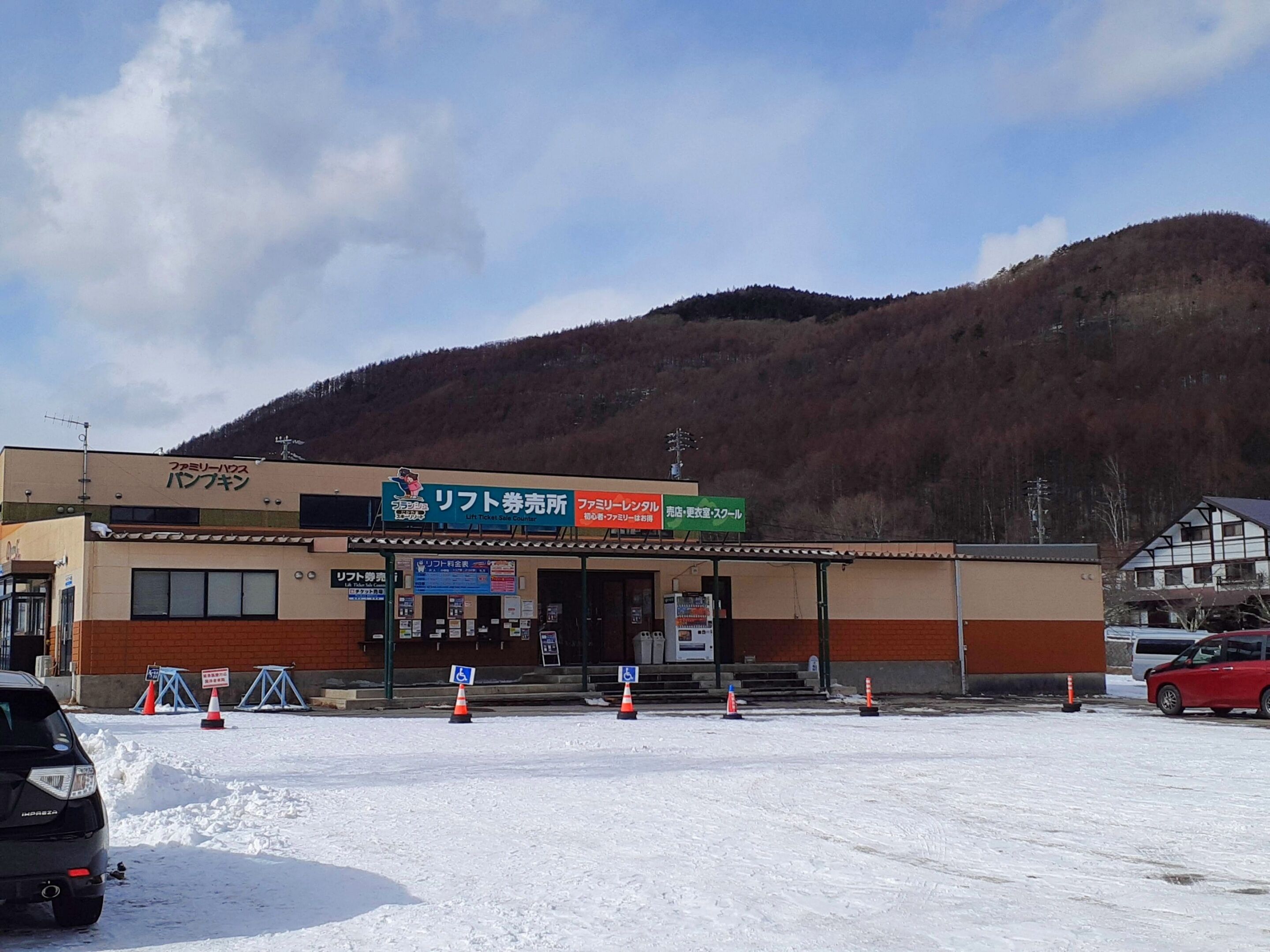 Um edifício com bilheteria e um estacionamento com neve.